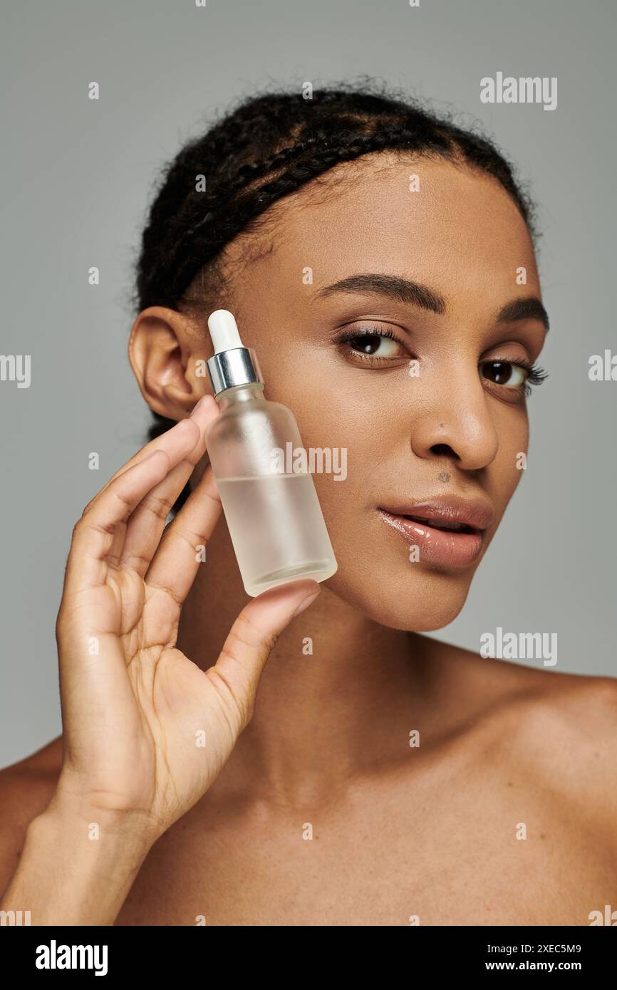 Beautiful young African American woman in strapless top holding serum to her face with focused ...