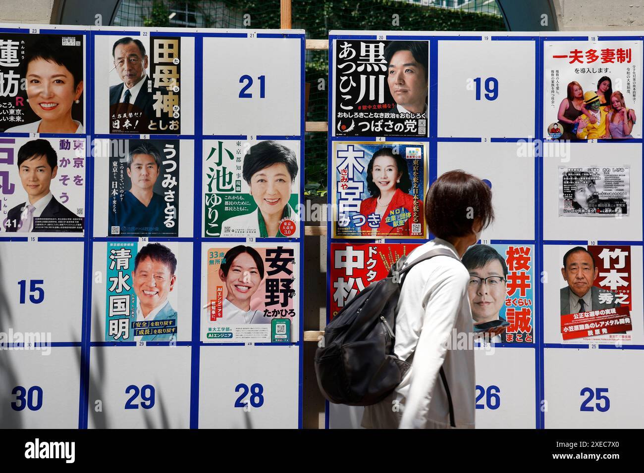 A woman walks past a candidates poster board for Tokyo gubernatorial ...