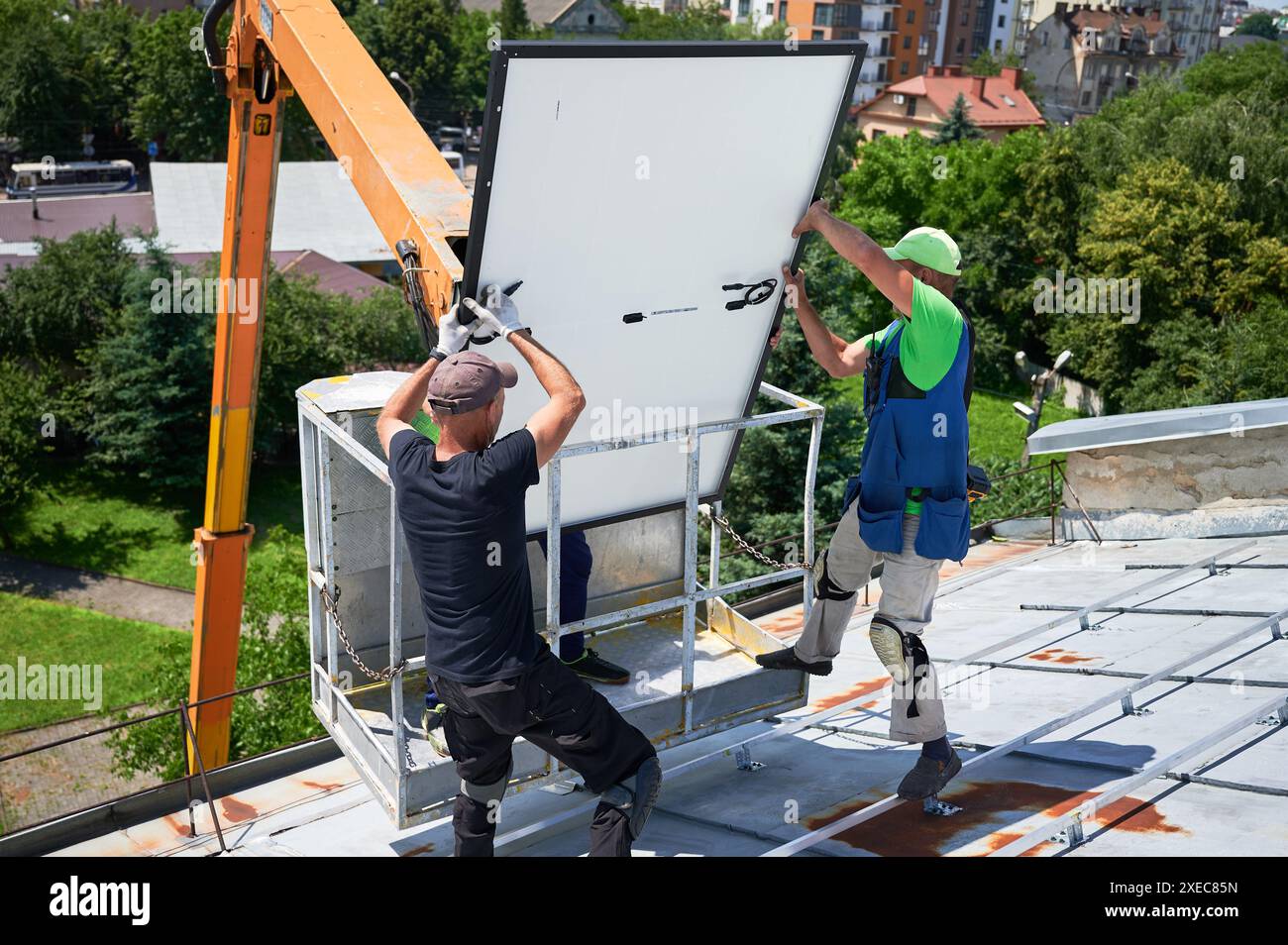Workers lifting up photovoltaic solar panel on metal rooftop of house ...