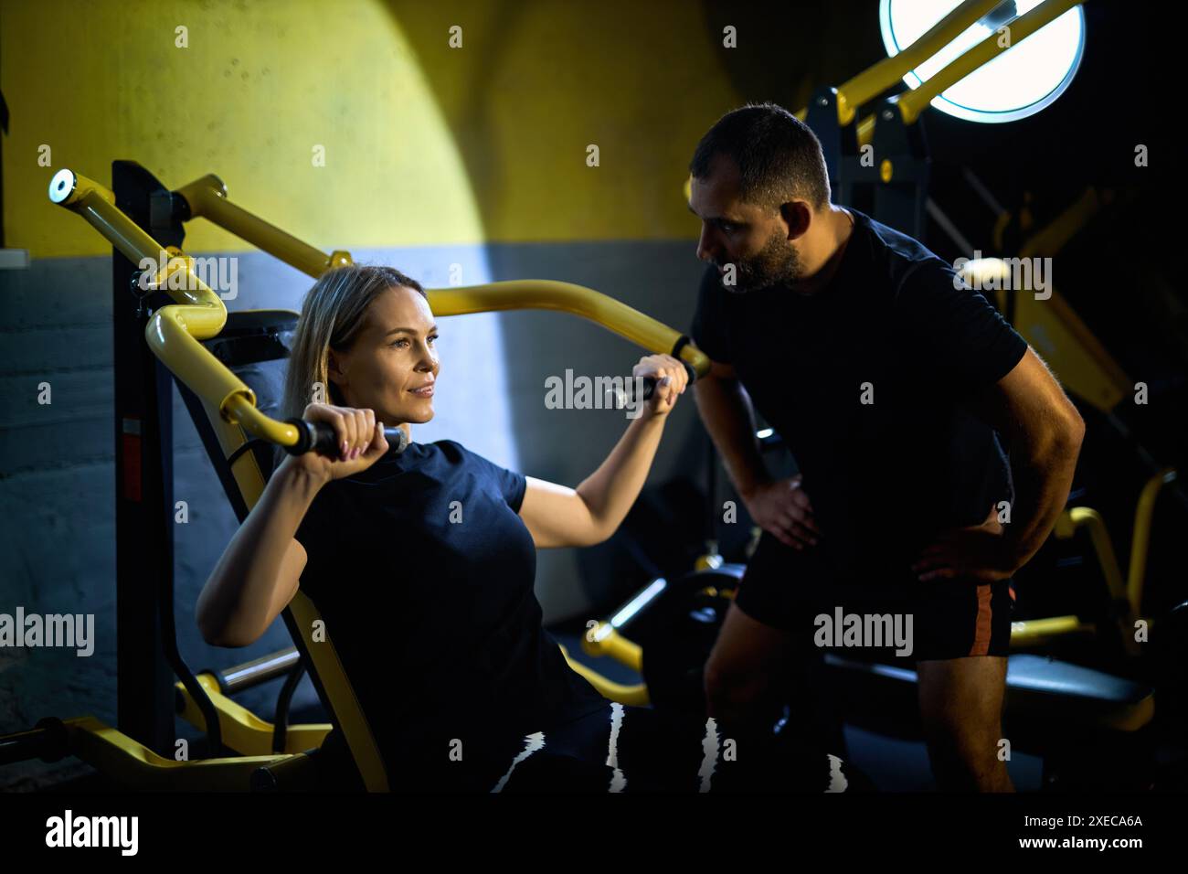 Personal coach assisting sportswoman in using machine during gym ...