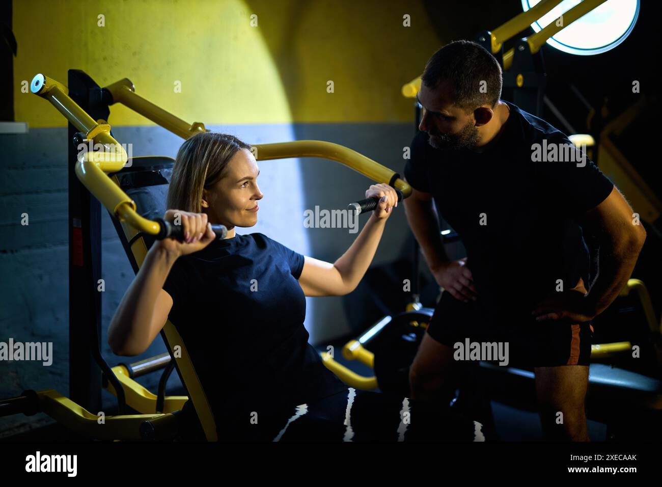 Personal coach assisting sportswoman in using machine during gym ...