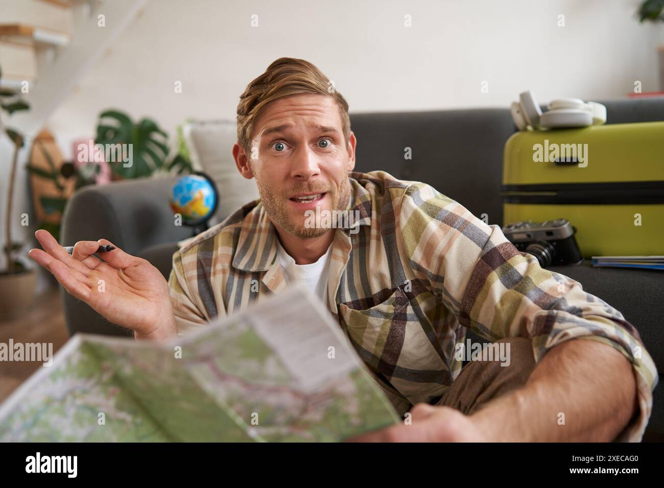 Portrait of man, tourist looking confused at travel map, shrugging ...