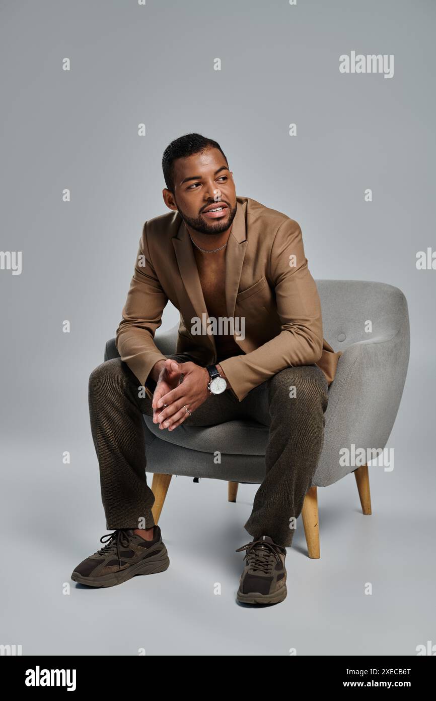 A man gracefully sits atop a gray chair in a contemplative pose Stock ...
