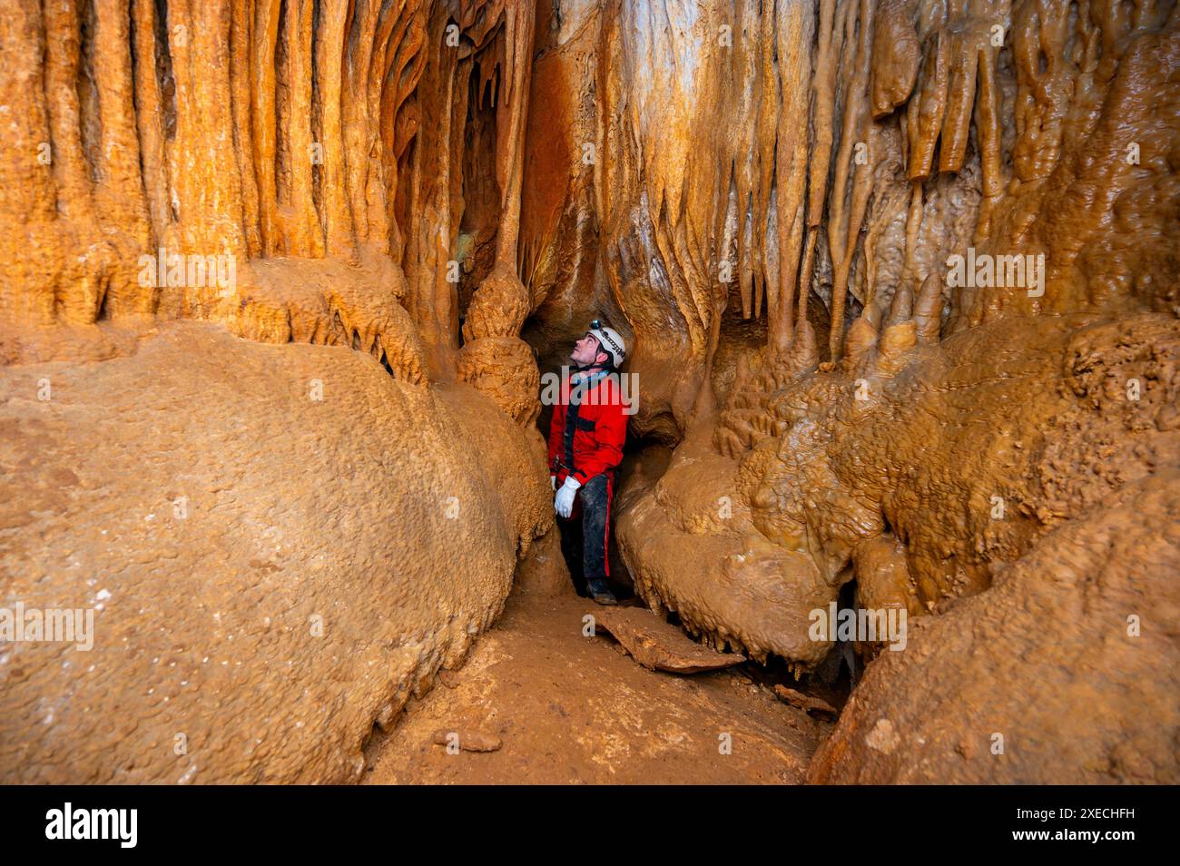A speleologist with helmet and headlamp exploring a cave with rich ...