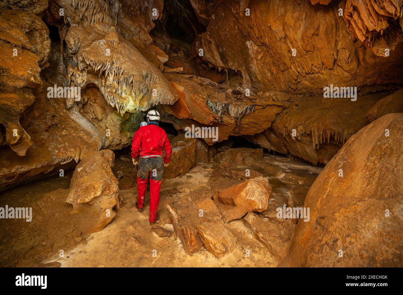 A speleologist with helmet and headlamp exploring a cave with rich ...