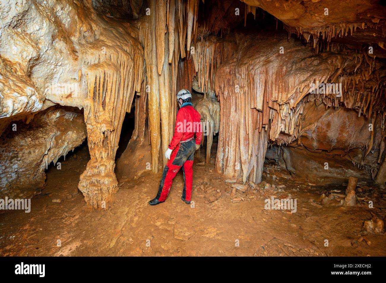 A speleologist with helmet and headlamp exploring a cave with rich ...