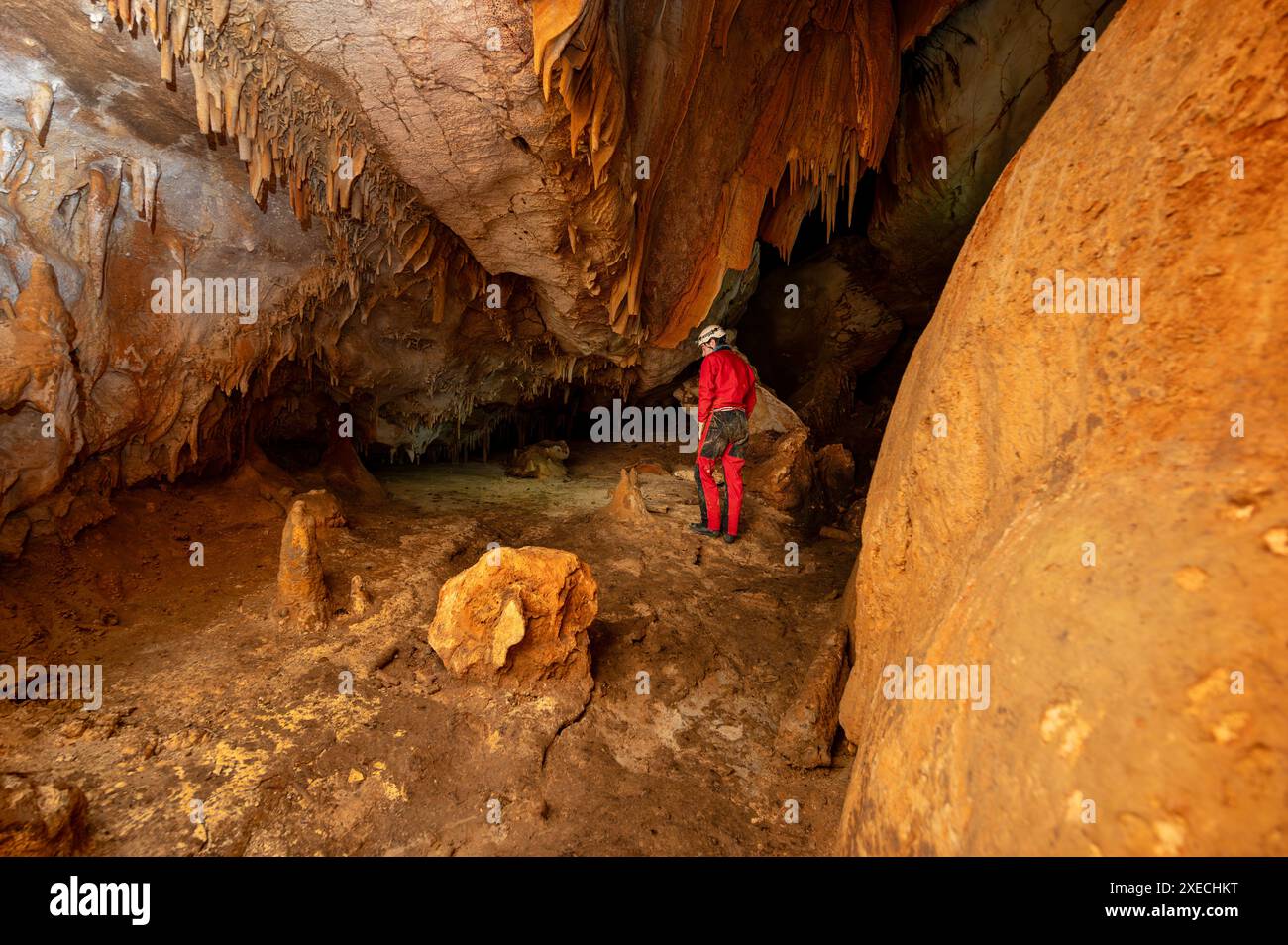 A speleologist with helmet and headlamp exploring a cave with rich ...