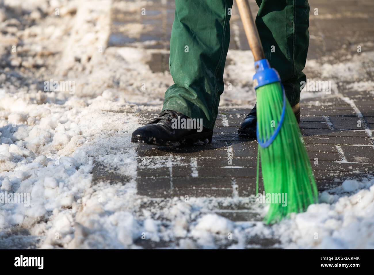 The close-up shot shows a manual worker sweeping the remaining snow off ...