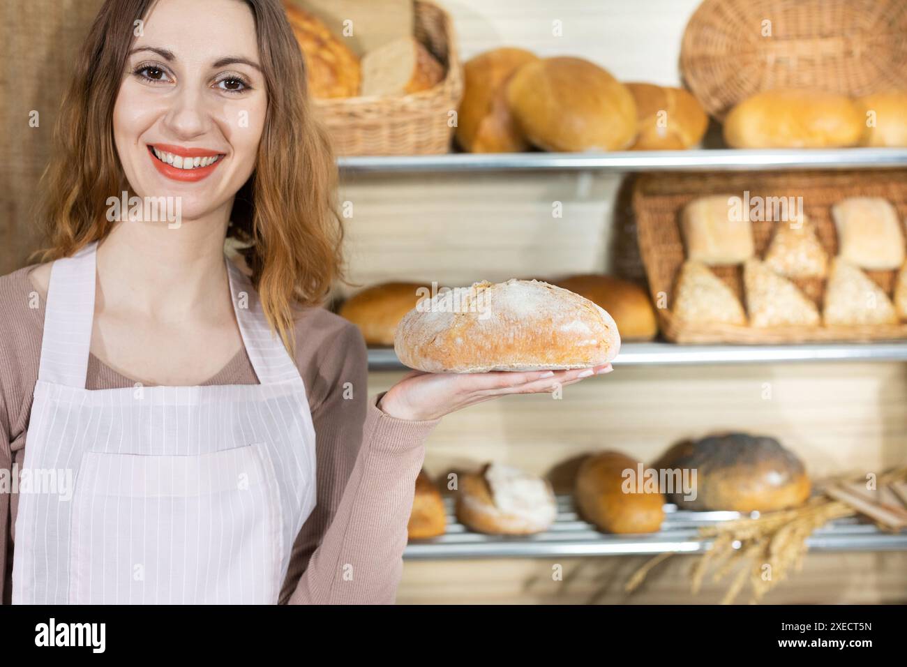 An attractive young saleswoman holds a loaf of bread in her hands ...