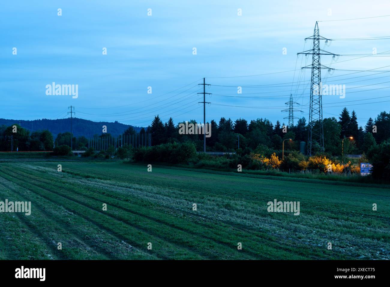 High voltage pylons with cabling at night behind a field. Yellow lights ...