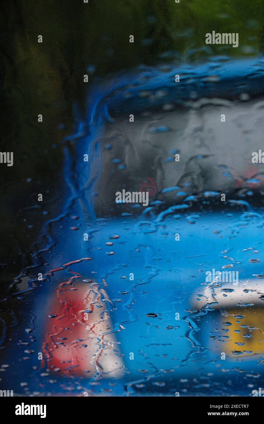 An empty blue car parked on the roadside, seen through a rain covered ...