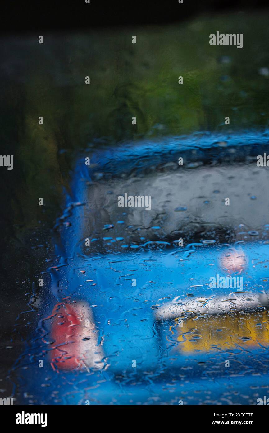 An empty blue car parked on the roadside, seen through a rain covered ...