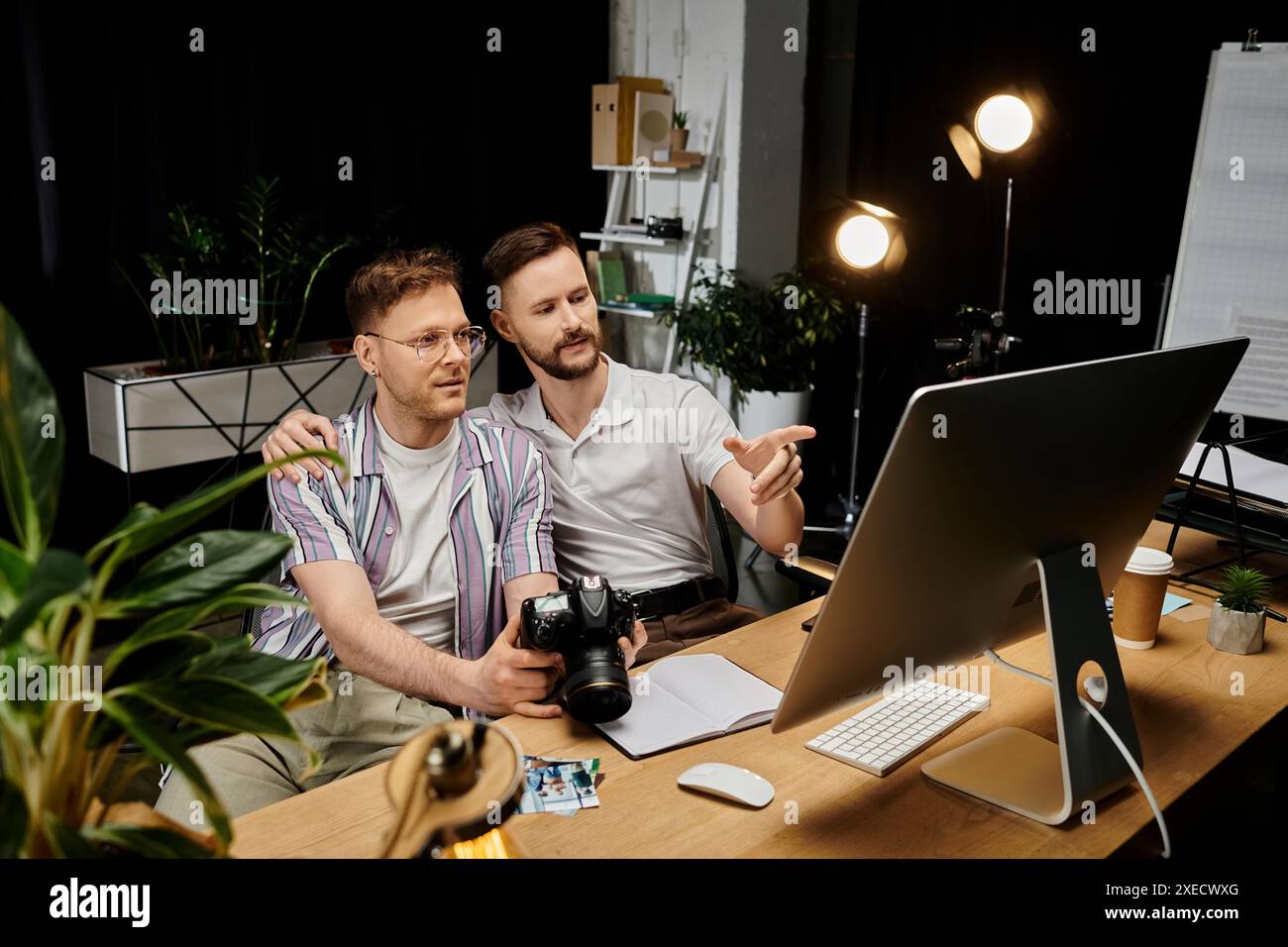 Two men in casual outfits working together at a desk with a computer ...