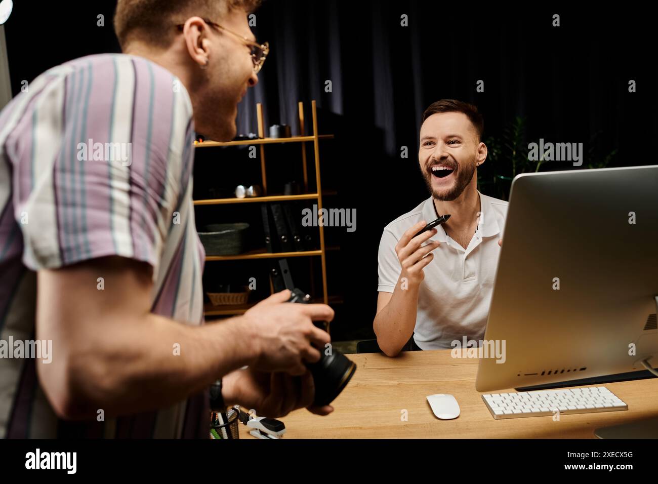 Two men, one laughing, work together in front of a computer Stock Photo ...