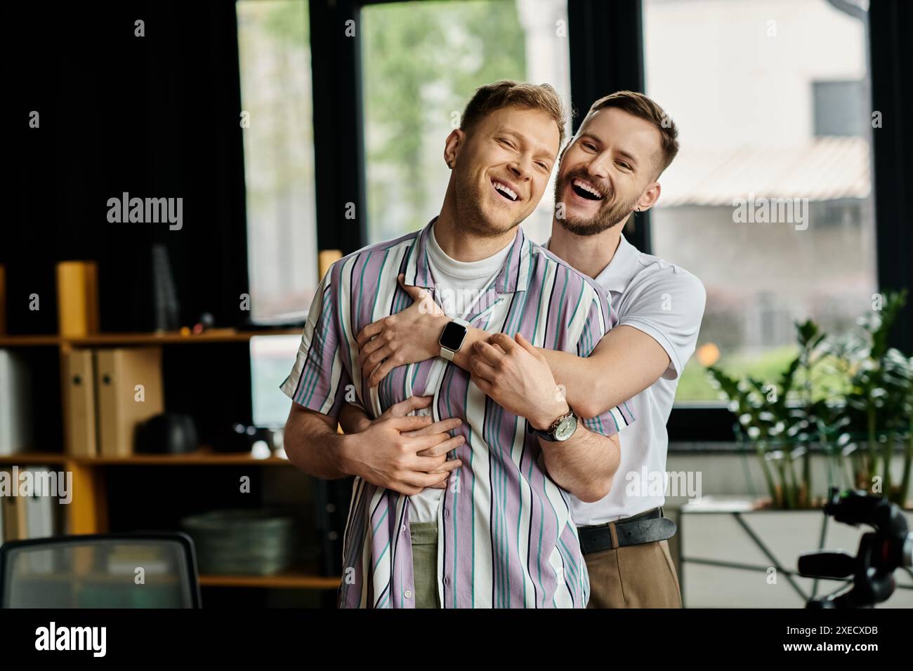 Two men in casual attire stand together in an office setting, engaged ...