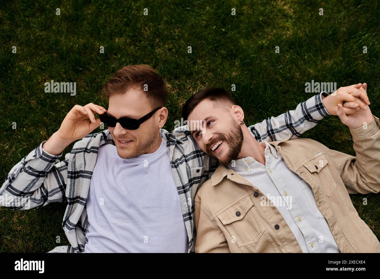 Two men in love, laying on a vibrant green field, enjoying each others ...