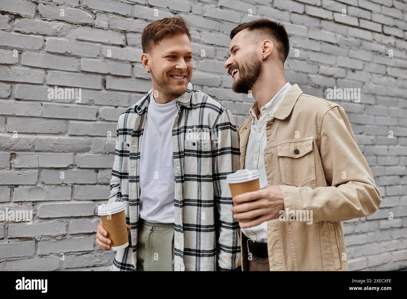 Two men in casual attire standing together, holding cups of coffee ...