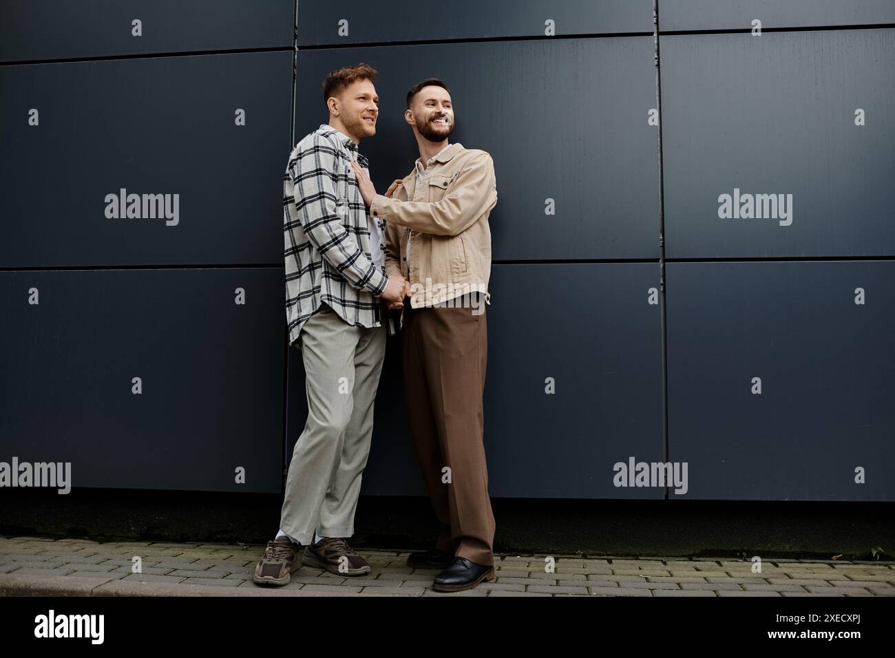 Two men in stylish attire standing near a wall, smiling Stock Photo - Alamy