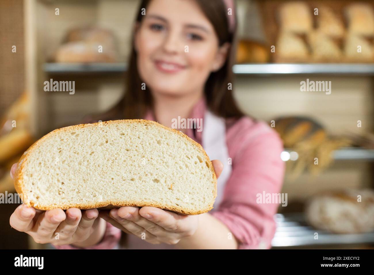 Against the backdrop of the bread shelves, a young attractive saleswoman shows a round cross ...