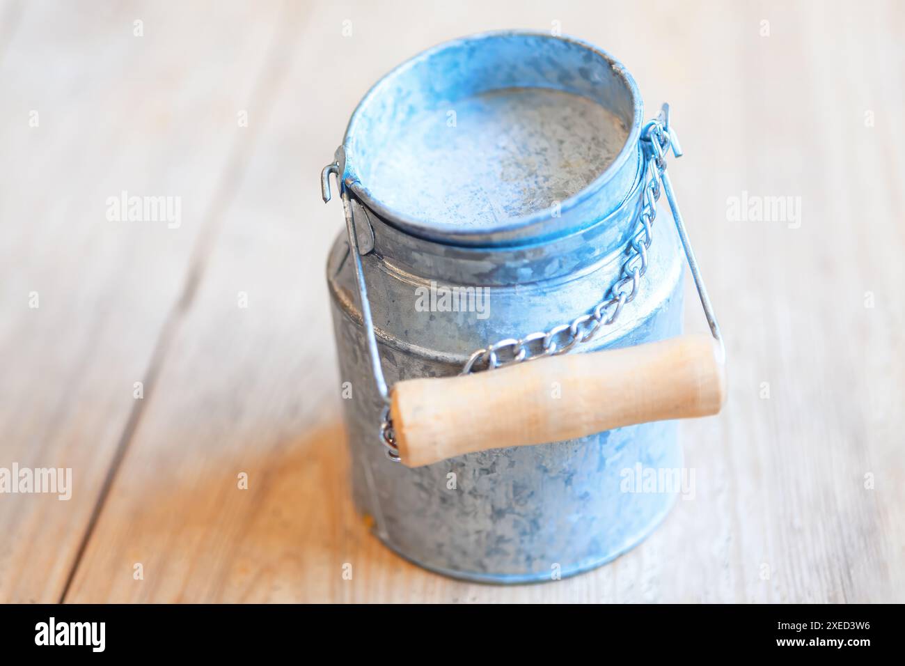 Silver metal bucket with a wooden handle sits on a wooden table. The ...