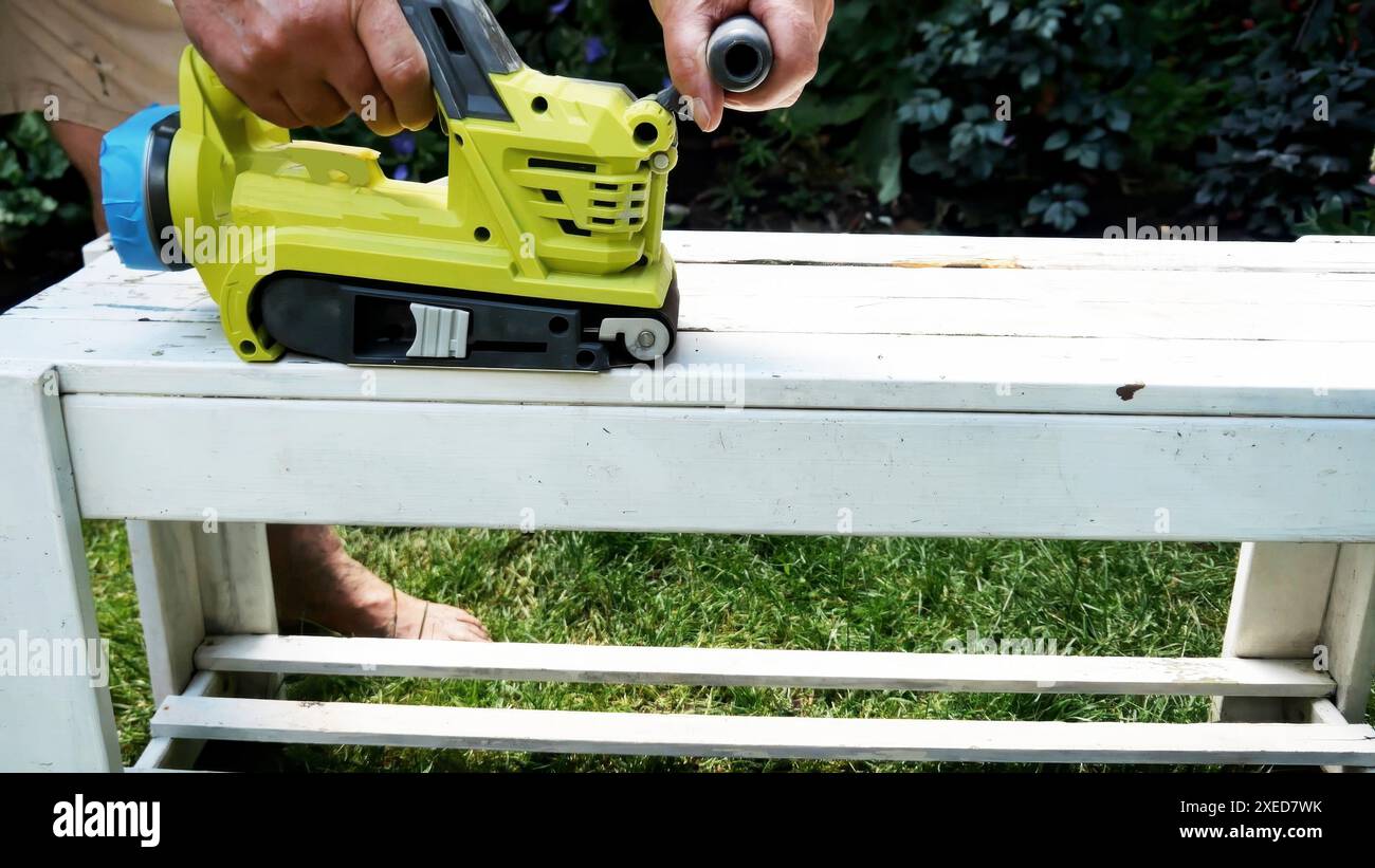 Hand-held battery powered belt sander to level the surface on garden ...