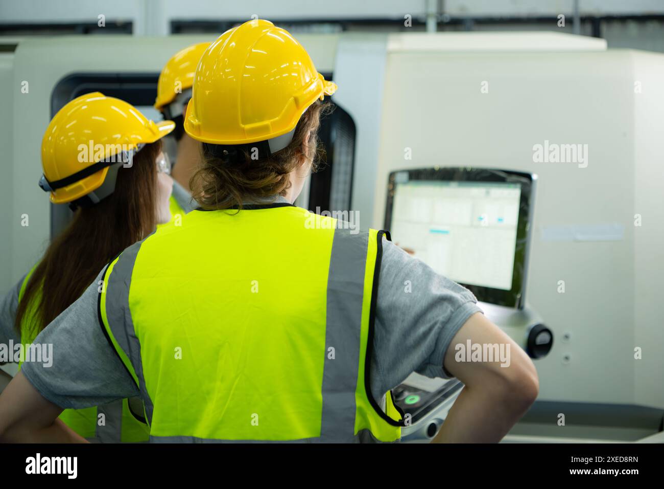 Back view of group young factory worker wearing a hard hat looking at a ...