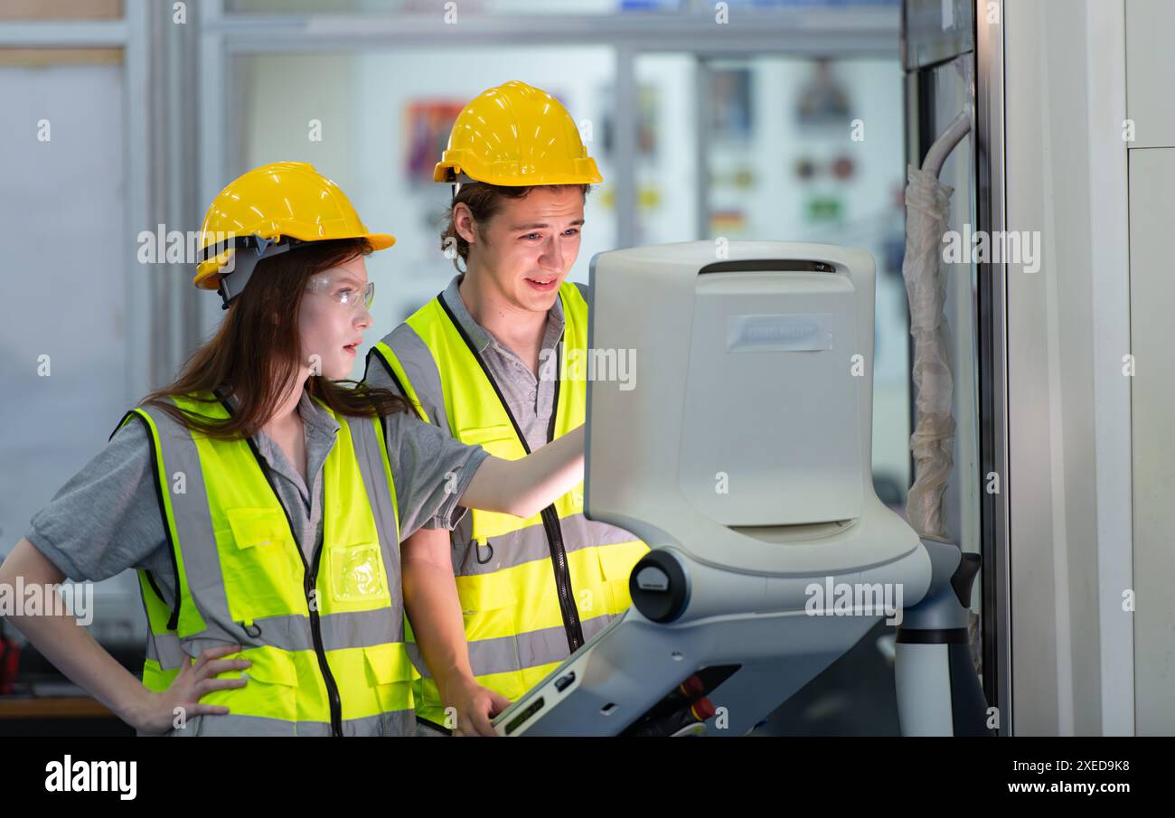 Both of young factory worker wearing a hard hat looking at a computer ...