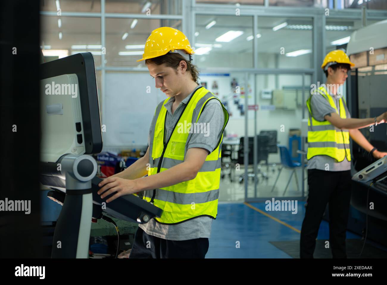 Young man factory worker wearing a hard hat looking at a computer ...