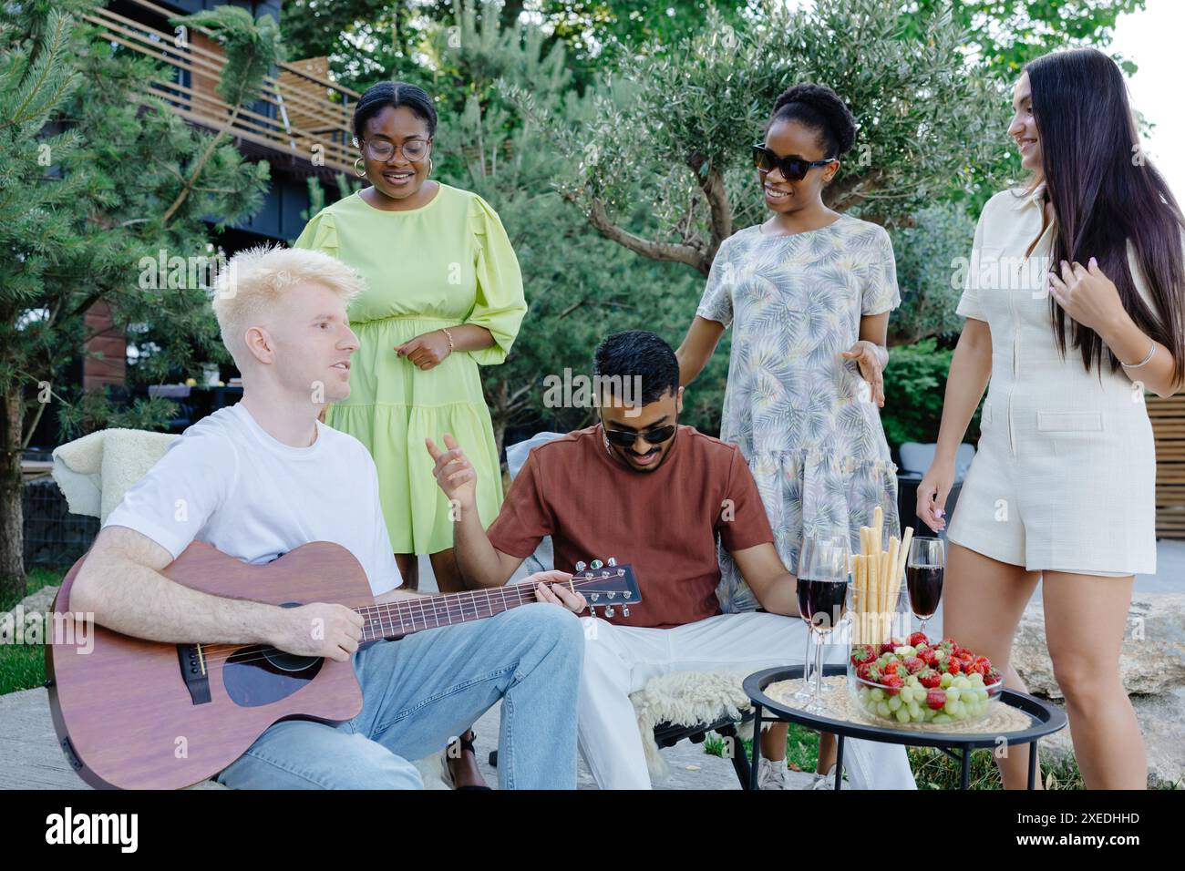 Multiracial group of friends is playing guitar, singing songs at dinner ...