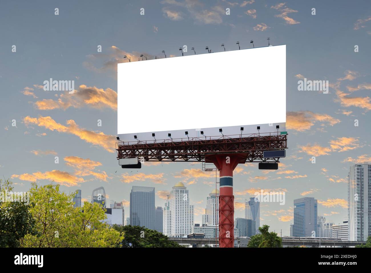 A large blank billboard stands in front of a city skyline. The city ...