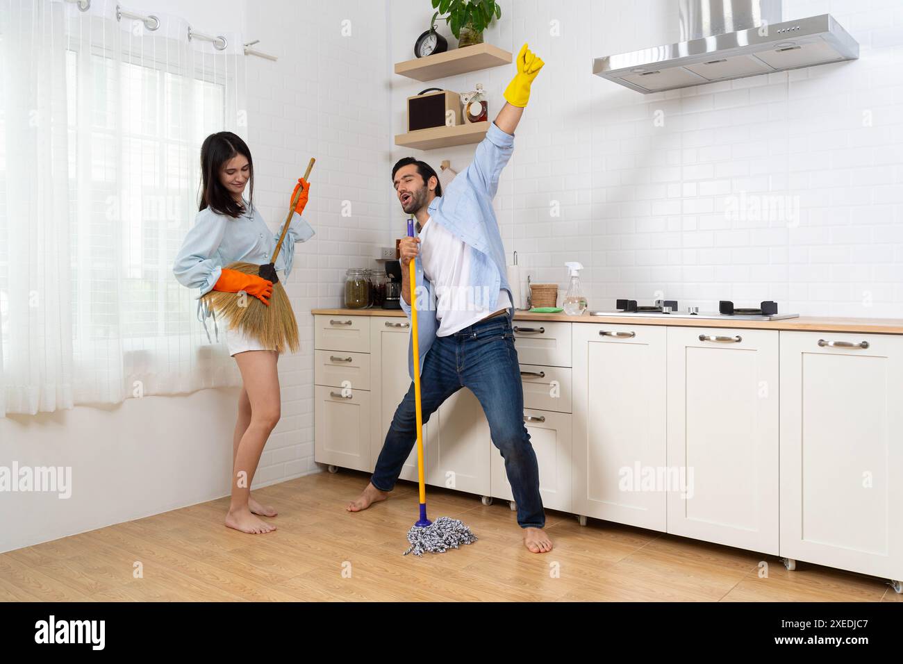 Joyful loving couple singing songs while cleaning kitchen, using broom ...