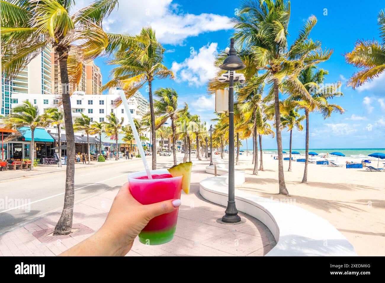 Seafront beach promenade with hand holding cocktail and palm trees on ...