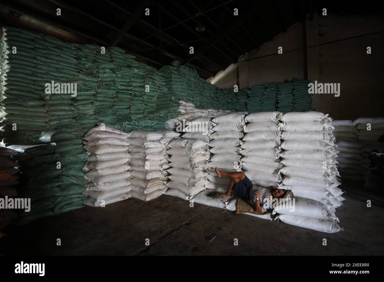 June 27, 2024: A worker rests on sacks of chemical fertilizer stored ...