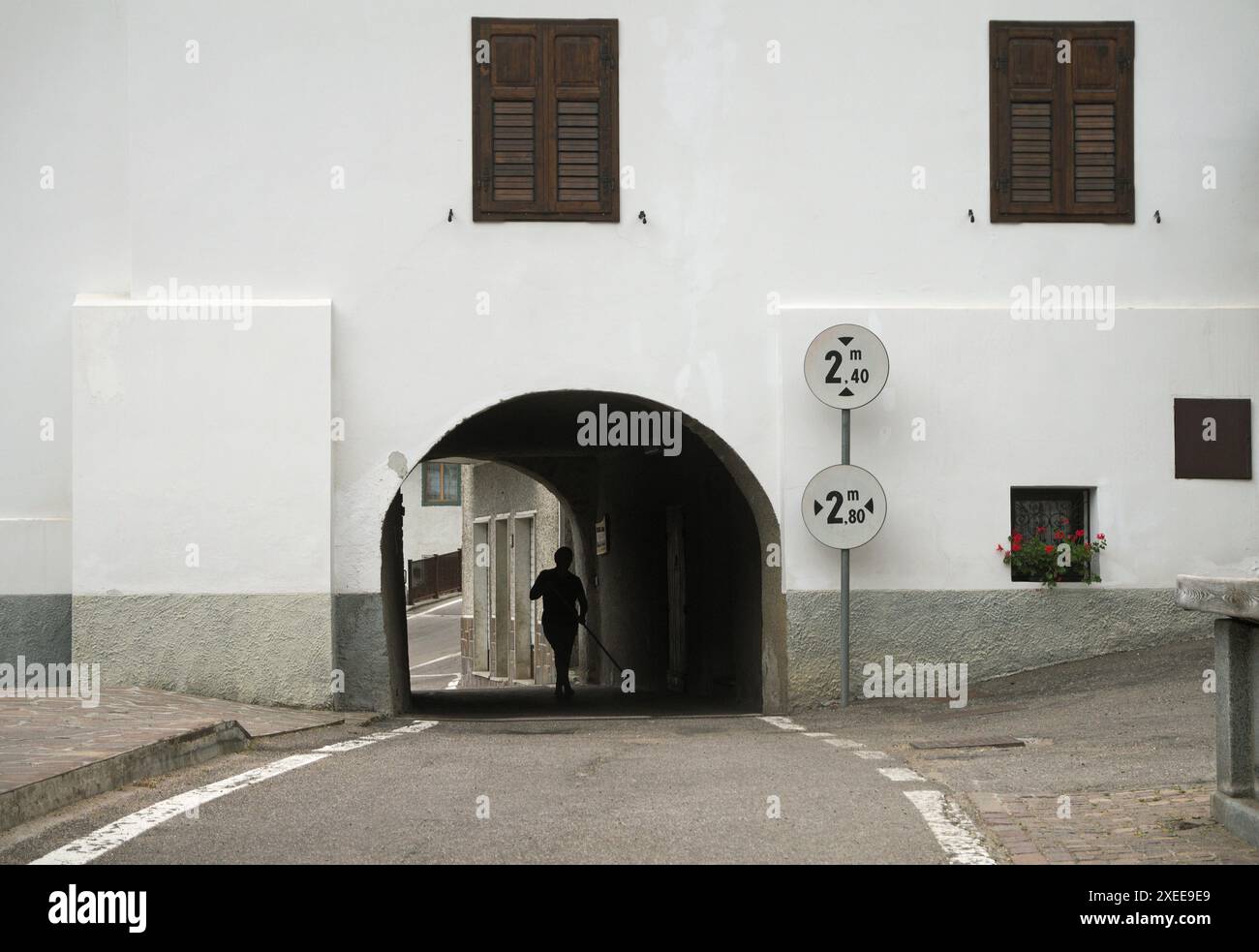 woman sweeping the street outside her house under a archway with width ...