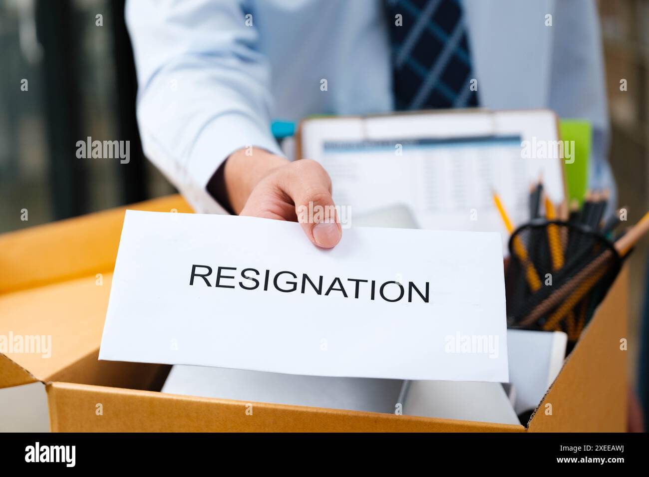 Man's hand presenting a resignation letter, office box with belongings ...