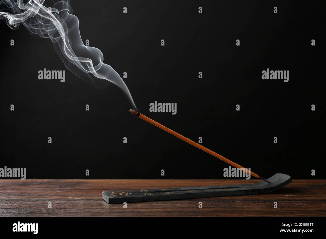 Aromatic incense stick smoldering in holder with Om signs on wooden ...