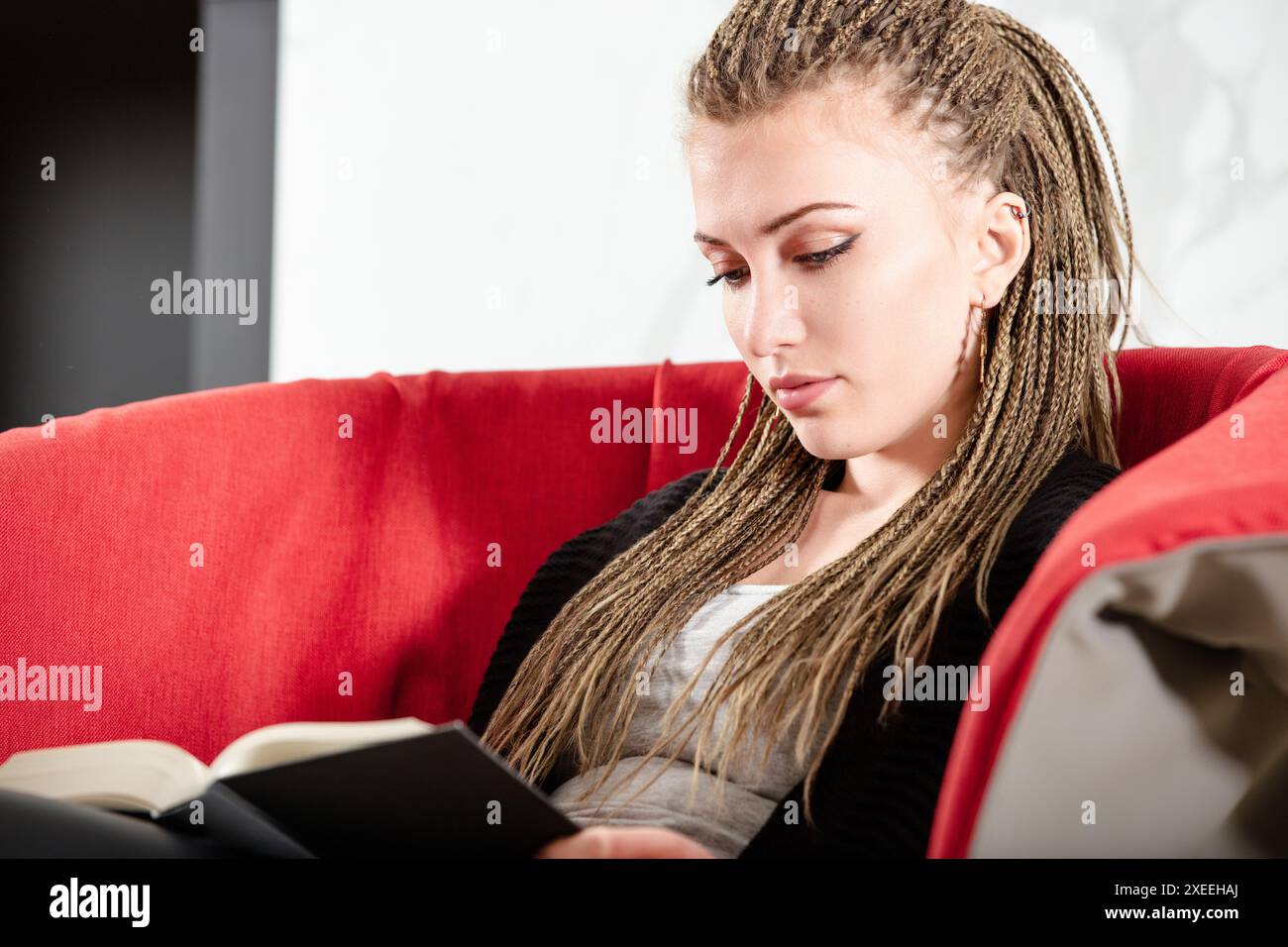 Young woman reading a book on a red sofa in a cozy living room, exuding ...