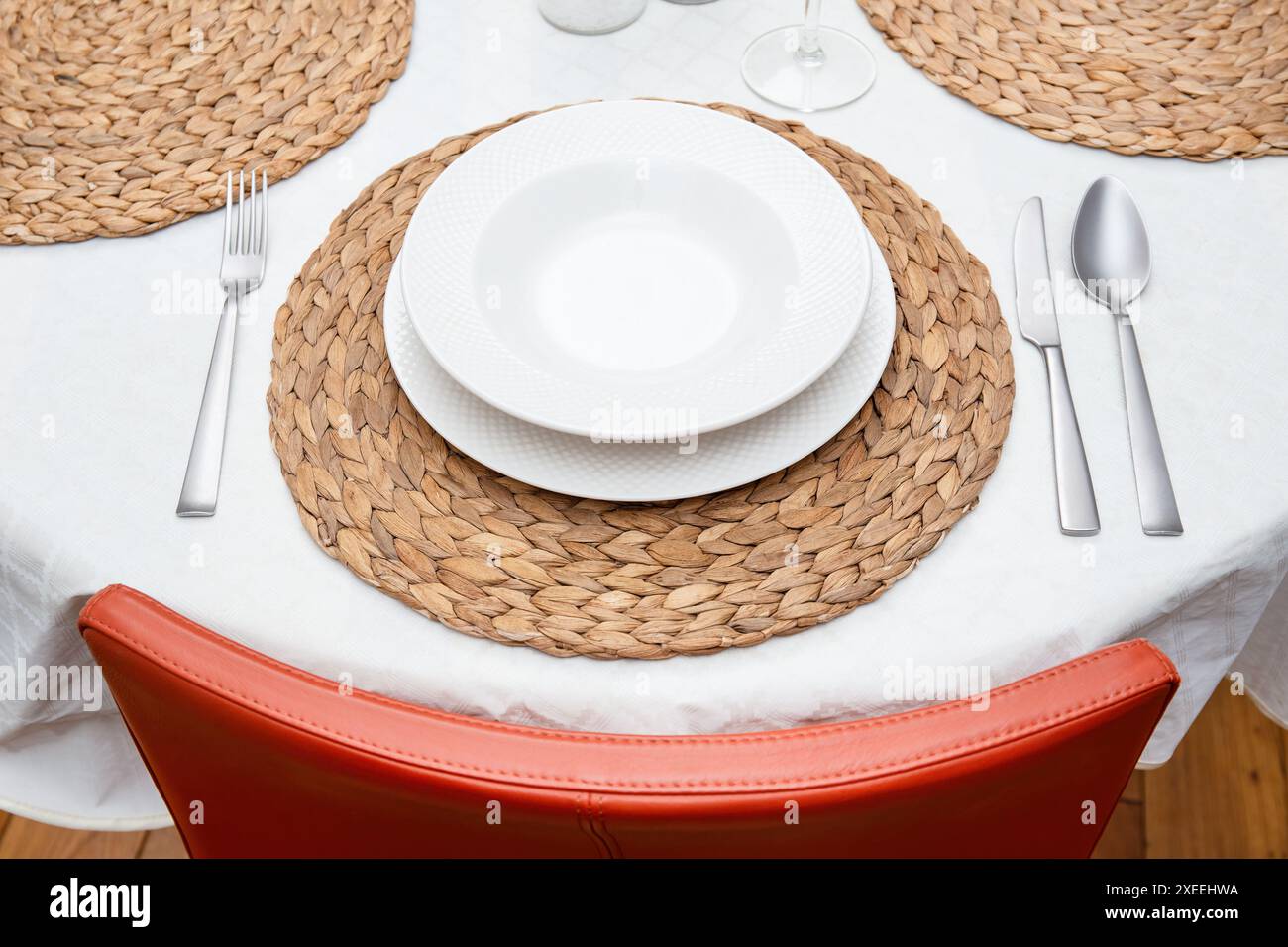 An elegant dinner table setting featuring white plates on woven ...