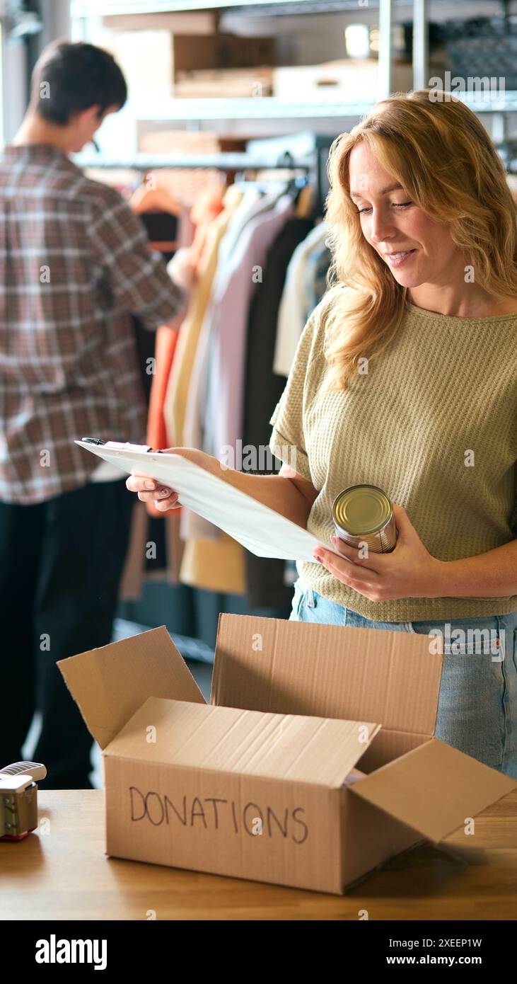 Male And Female Charity Volunteers Working Sorting Through Donations Of ...