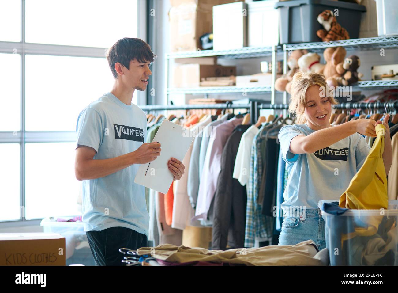 Male And Female Charity Volunteers Working Sorting Through Donations Of ...