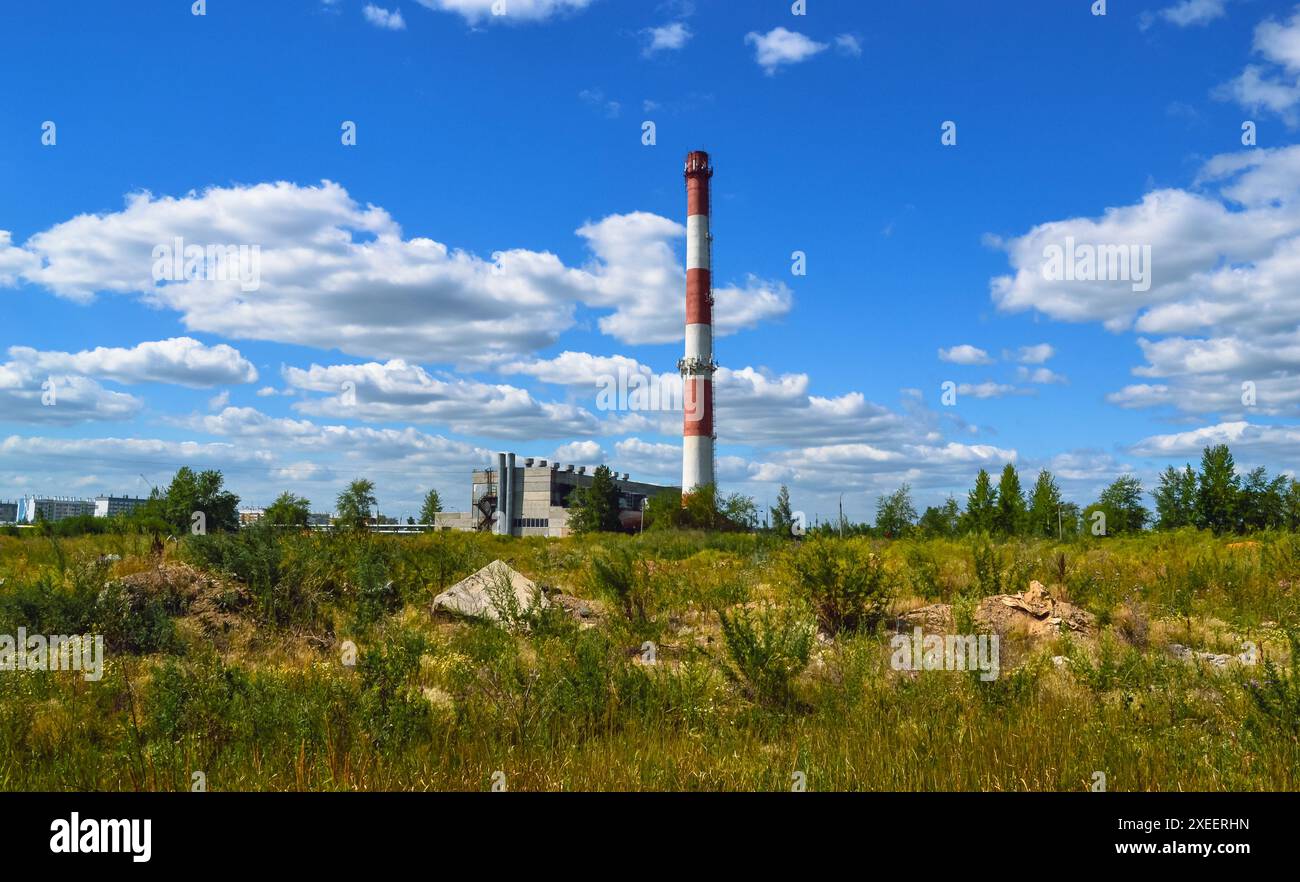 A wild field and a tall striped red and white chimney of a boiler house ...
