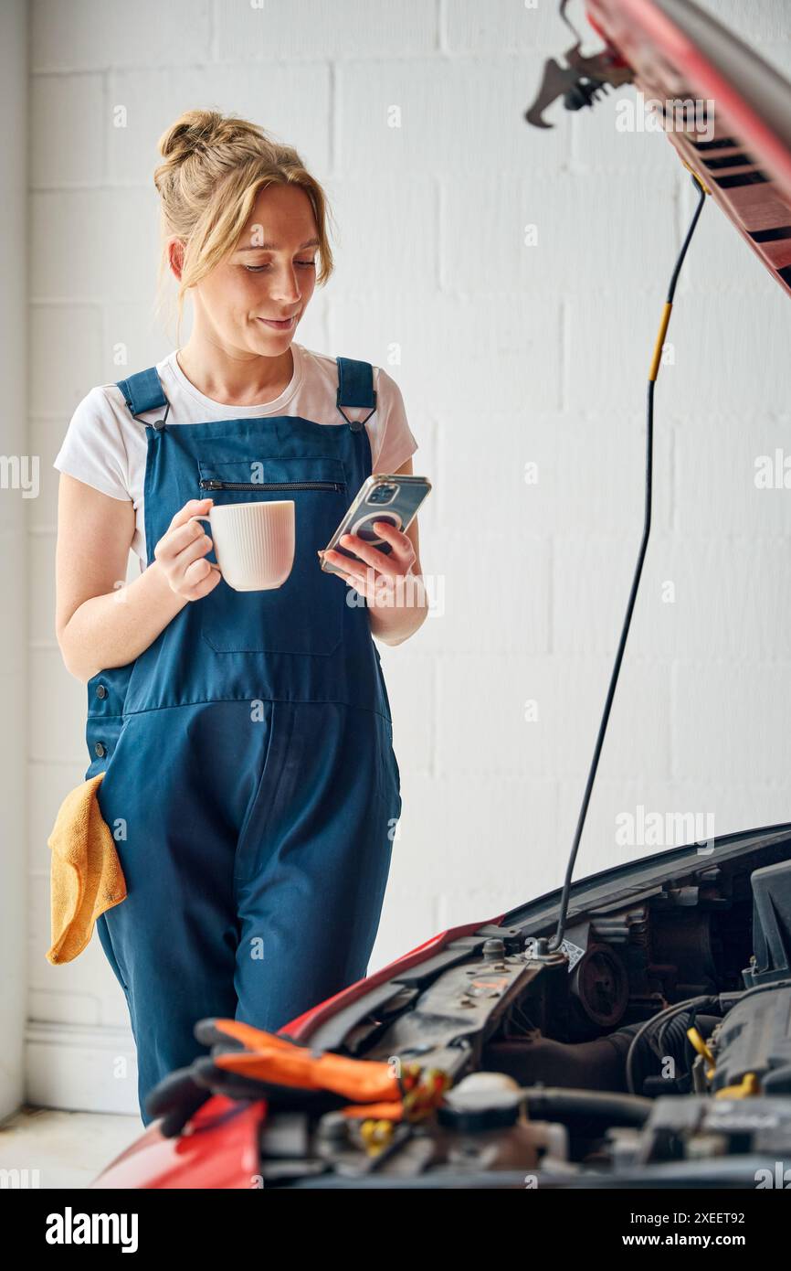 Female Car Auto Mechanic Looking At Mobile Phone On Coffee Break In ...