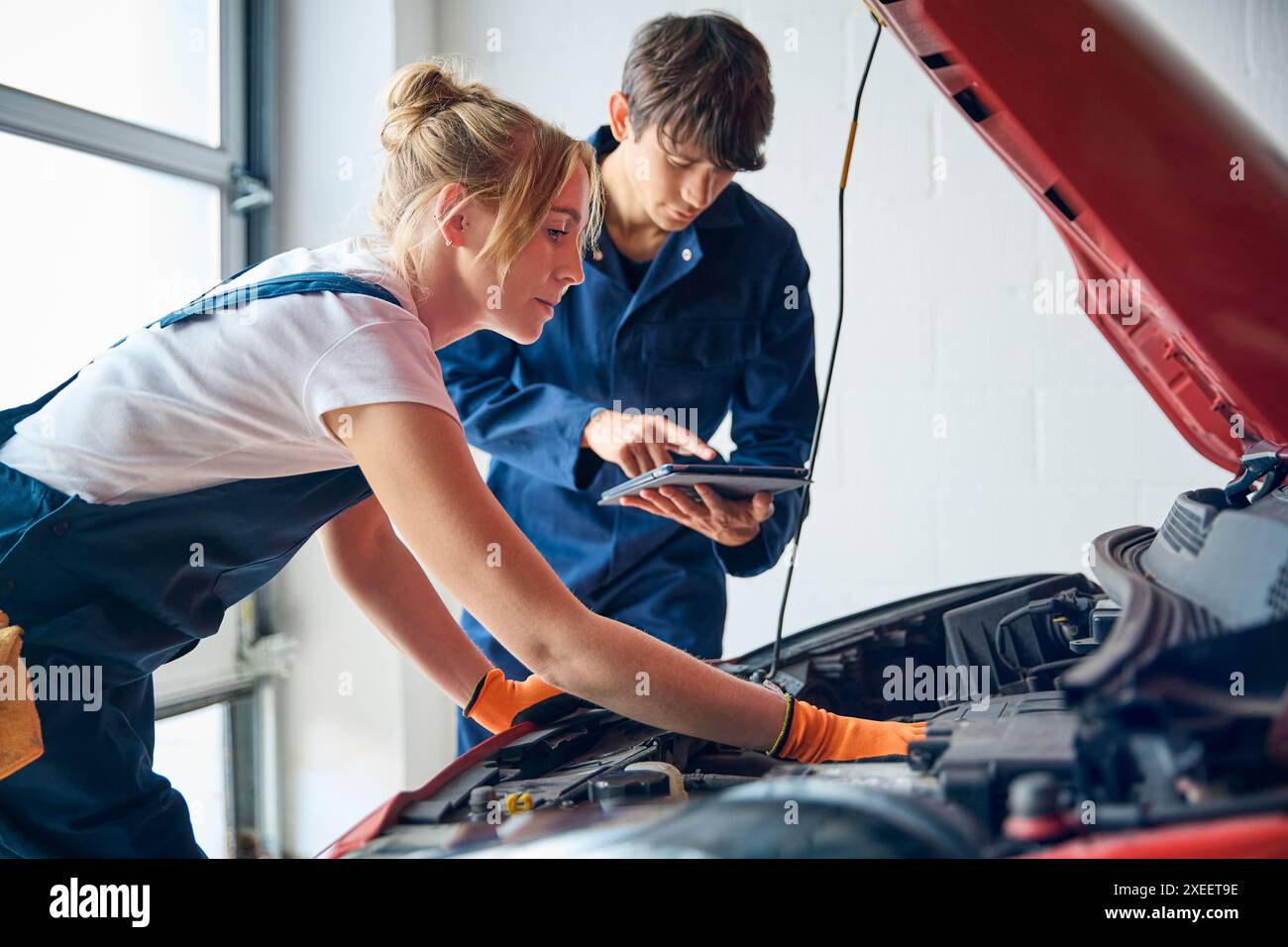 Female Car Auto Mechanic With Trainee Looking Under Bonnet Of Car Using ...