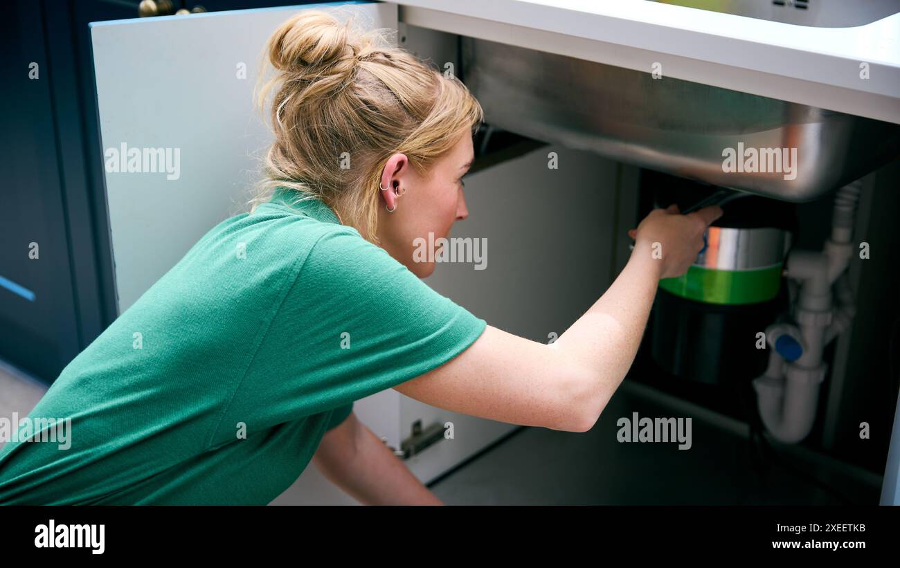 Female Plumber Fixing Waste Disposal Unit In Domestic Kitchen Sink ...