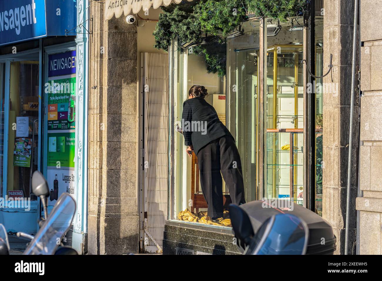 Businesswoman in black suit cleaning shop window on a sunny day in ...