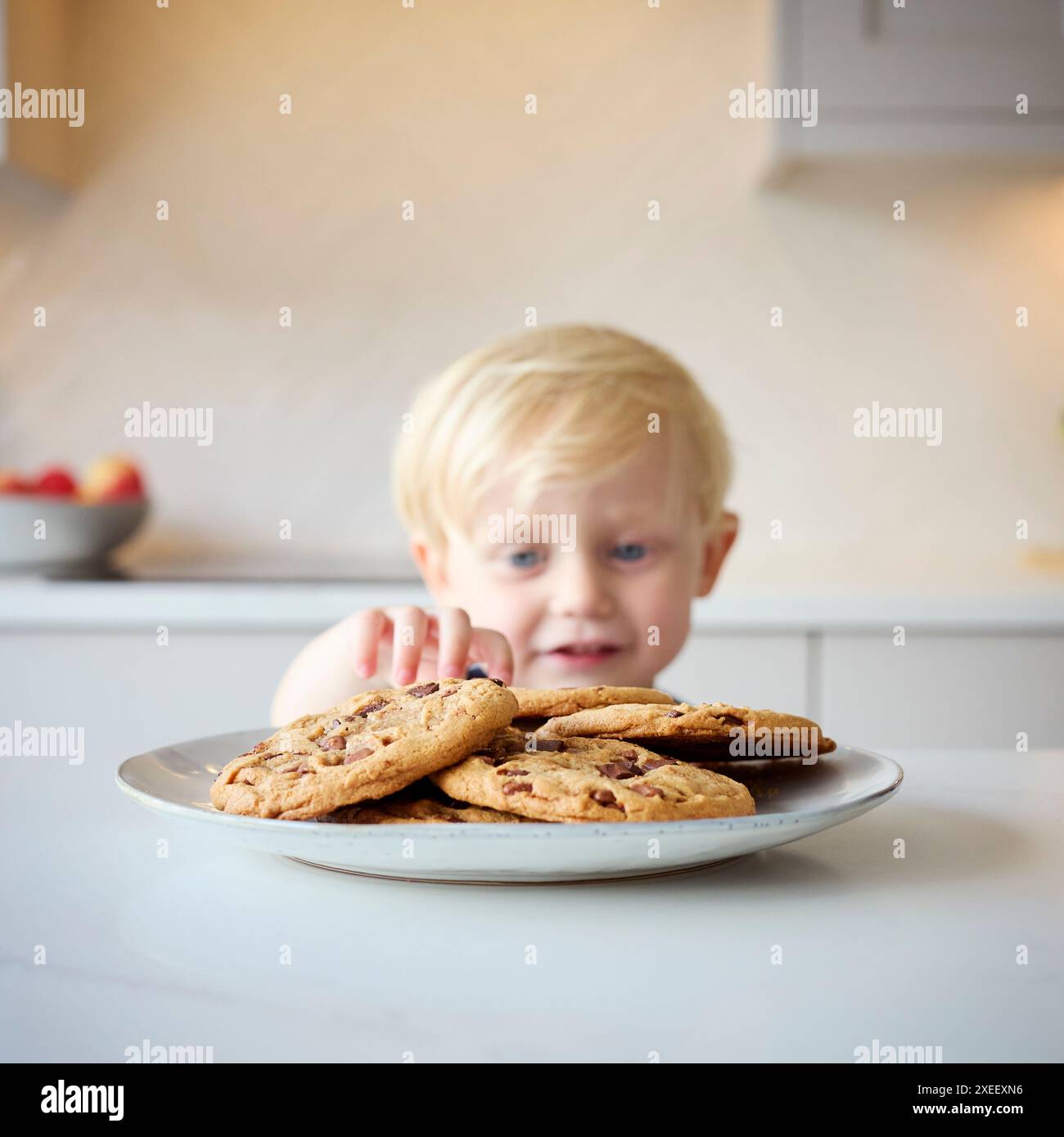 Mischievous Young Boy Taking Giant Cookie From Plate In Kitchen At Home ...
