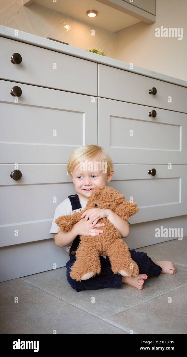 Smiling Young Boy Hugging Teddy Bear Sitting On Floor At Home In ...