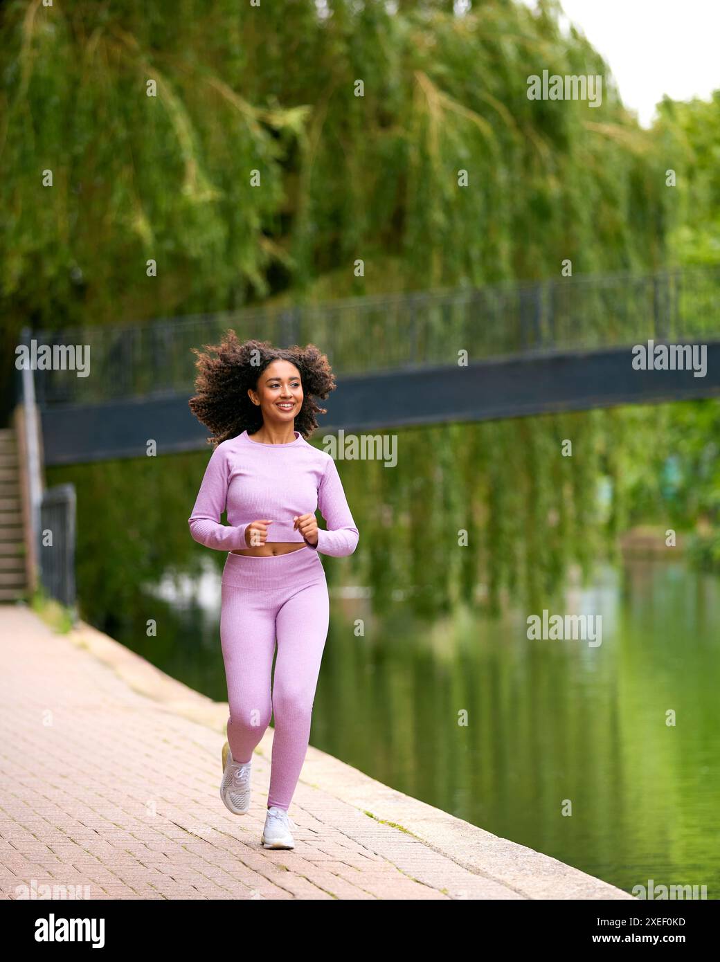 Woman Wearing Fitness Clothing Running Along Path By River In Urban ...