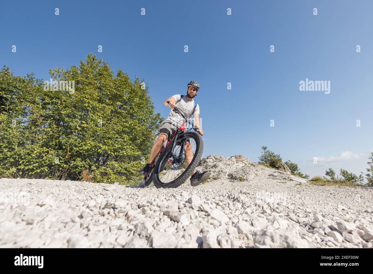 Male electric mountain bike rider going downhill and braking on a hilly rocky trail, low-angle ...