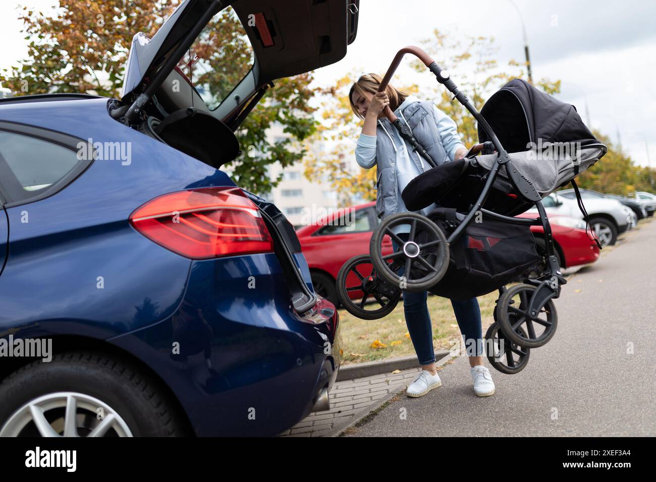 Young mother driver puts a baby stroller into the luggage compartment ...